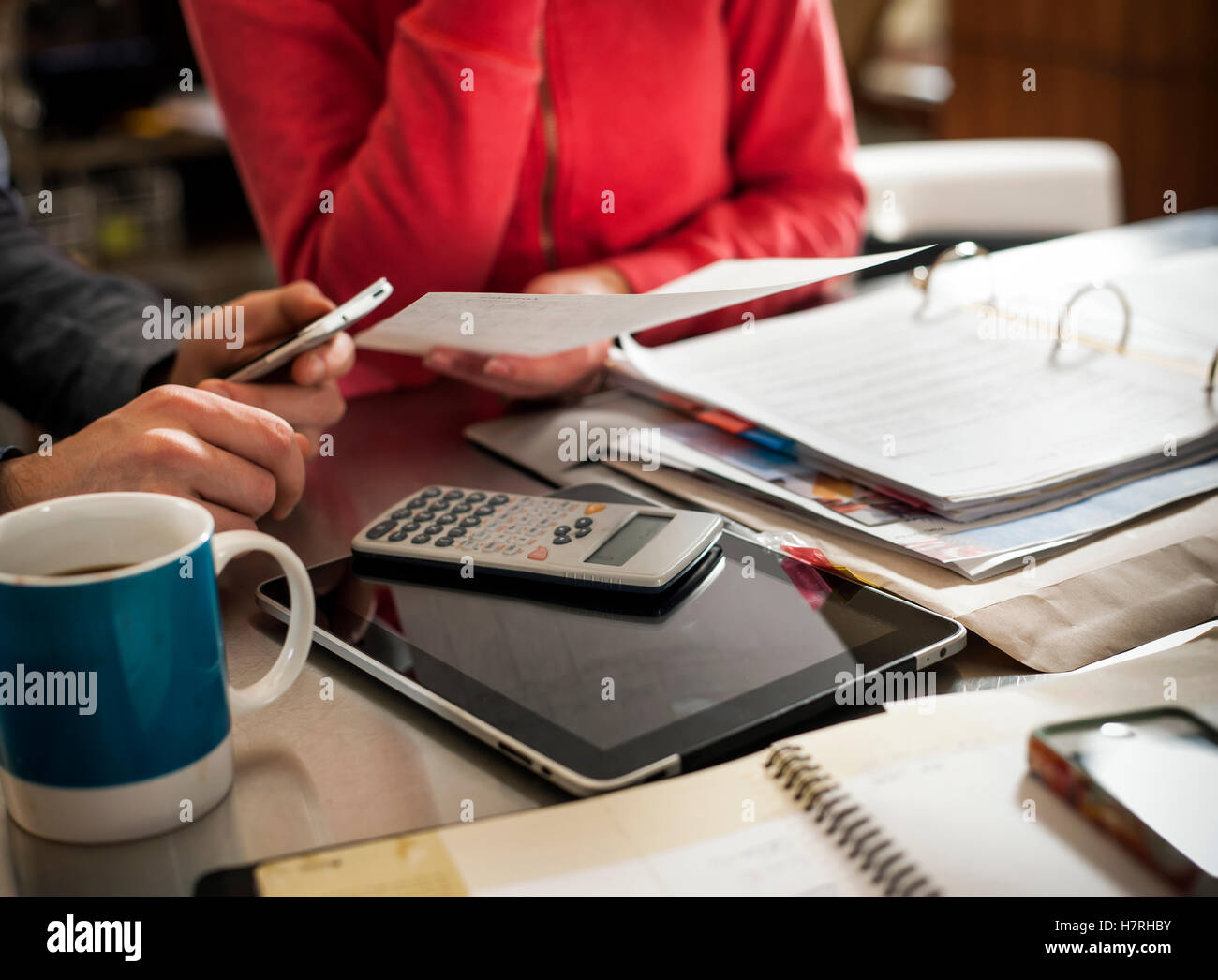 A man and woman sit at the kitchen table full of documents, calculator ...