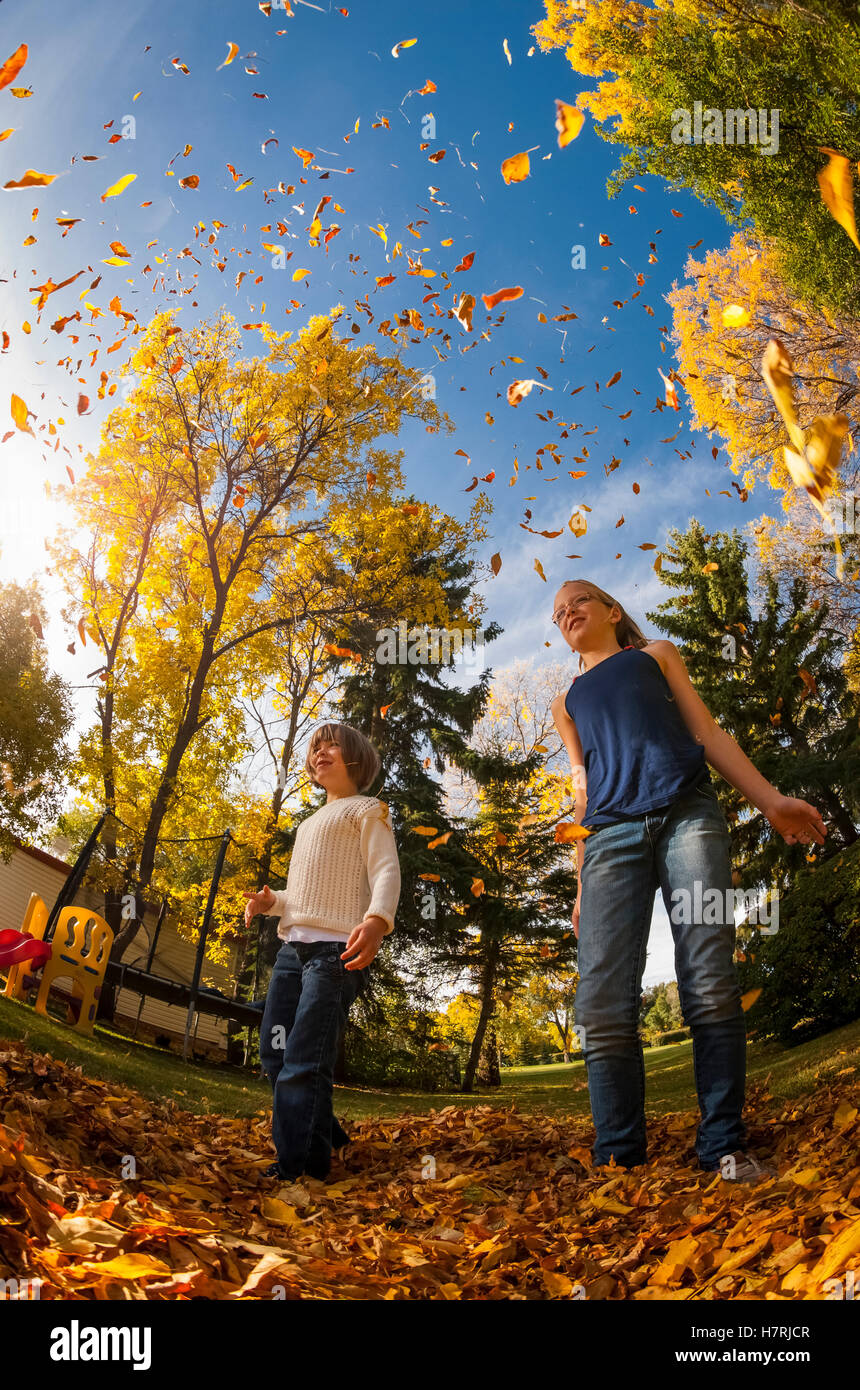 Sisters standing in a pile of leaves in autumn and throwing leaves into ...