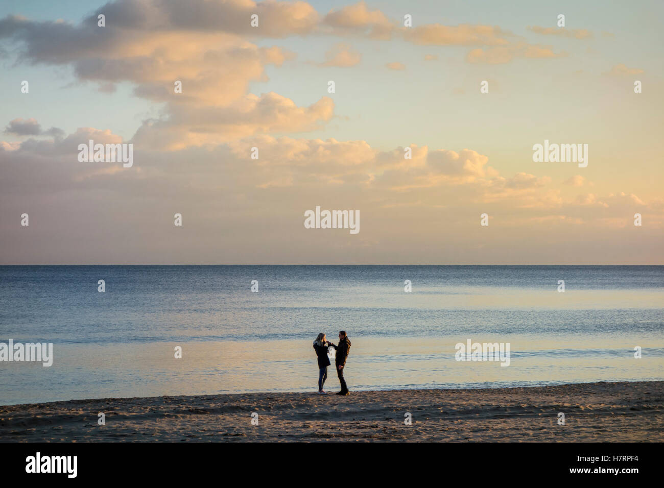 A couple alone enjoy the late afternoon sunlight on the beach at ...