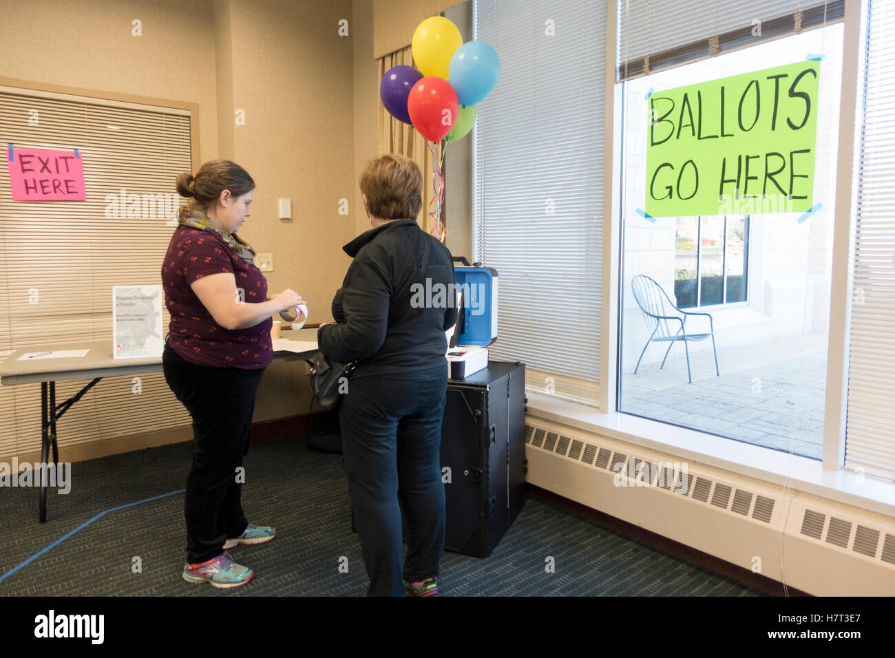Attendant taking "I Voted" sticker from roll as voter places voting ...