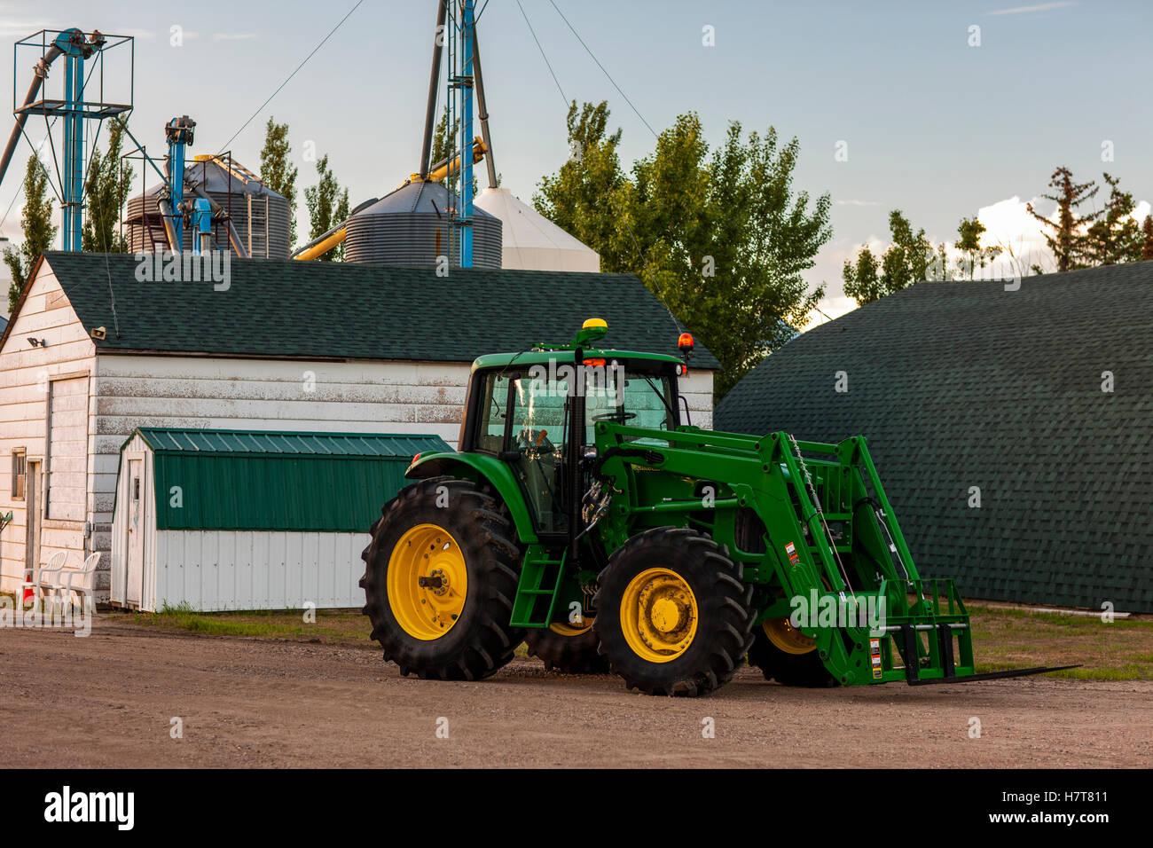 A green tractor sits on a farm outside a barn and silos; Herschel ...