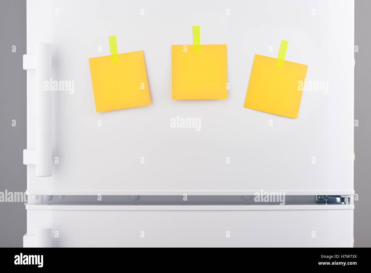 Three blank yellow paper notes attached with yellow stickers on white ...