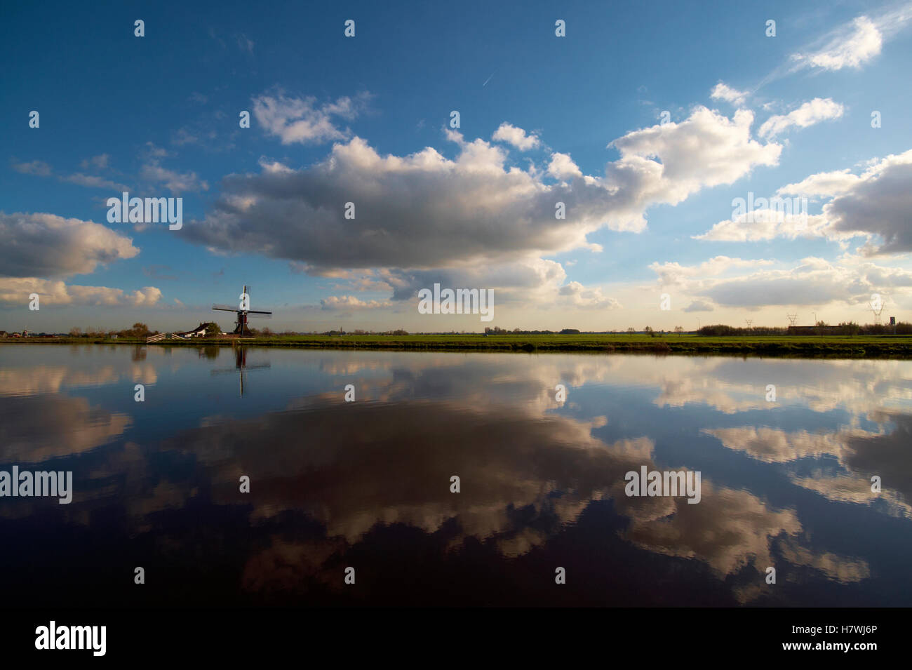 Polder landscape with windmill and cloudy sky reflected in the water ...