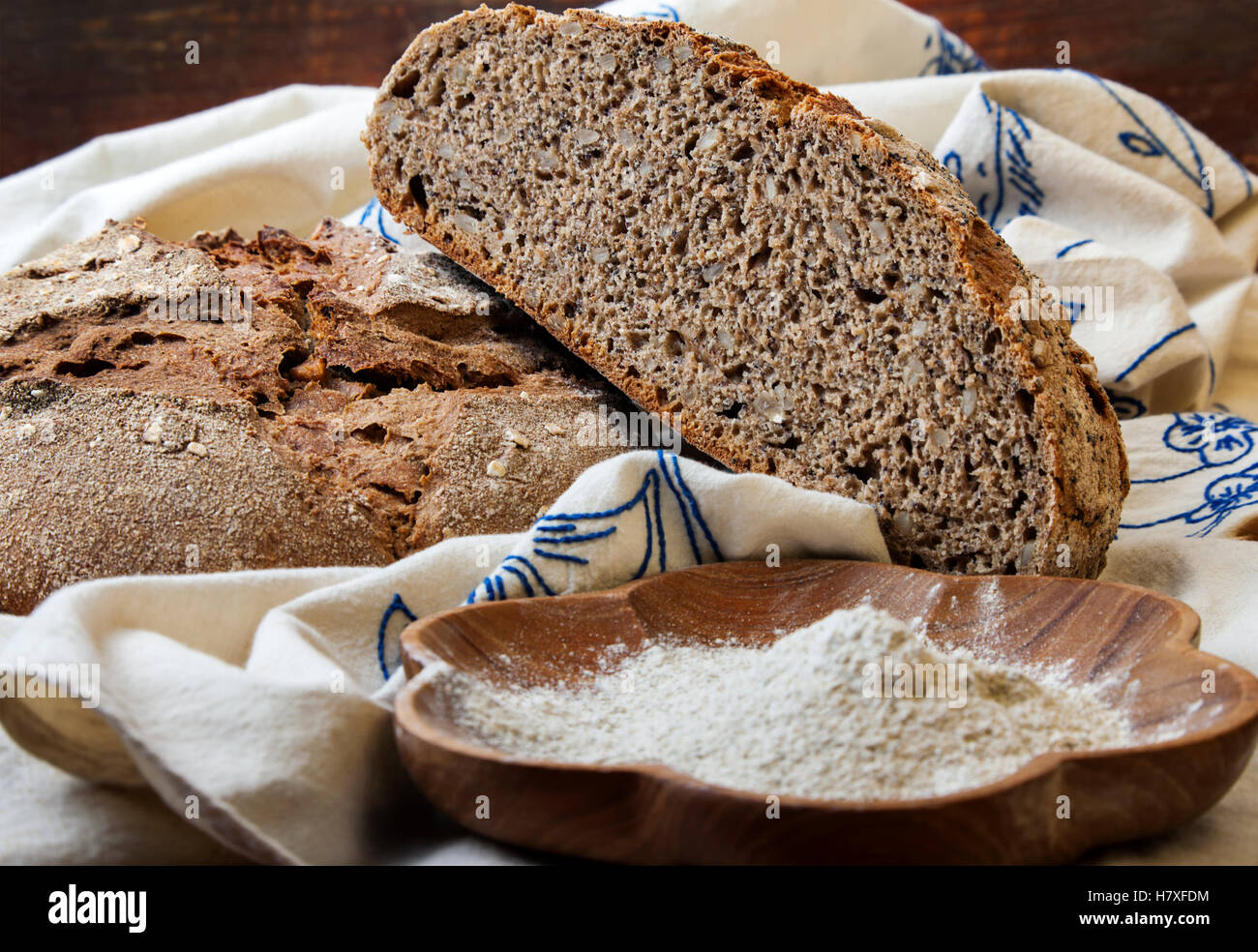 Sliced whole grain bread and a wooden cup of flour on a fabric cover ...