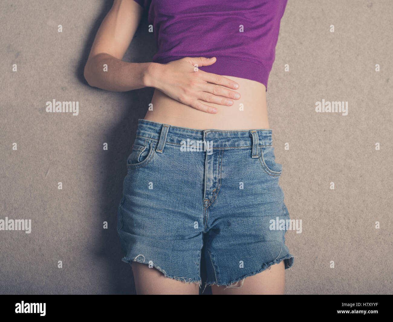 A young woman is relaxing at home on the carpet with her hand on her ...