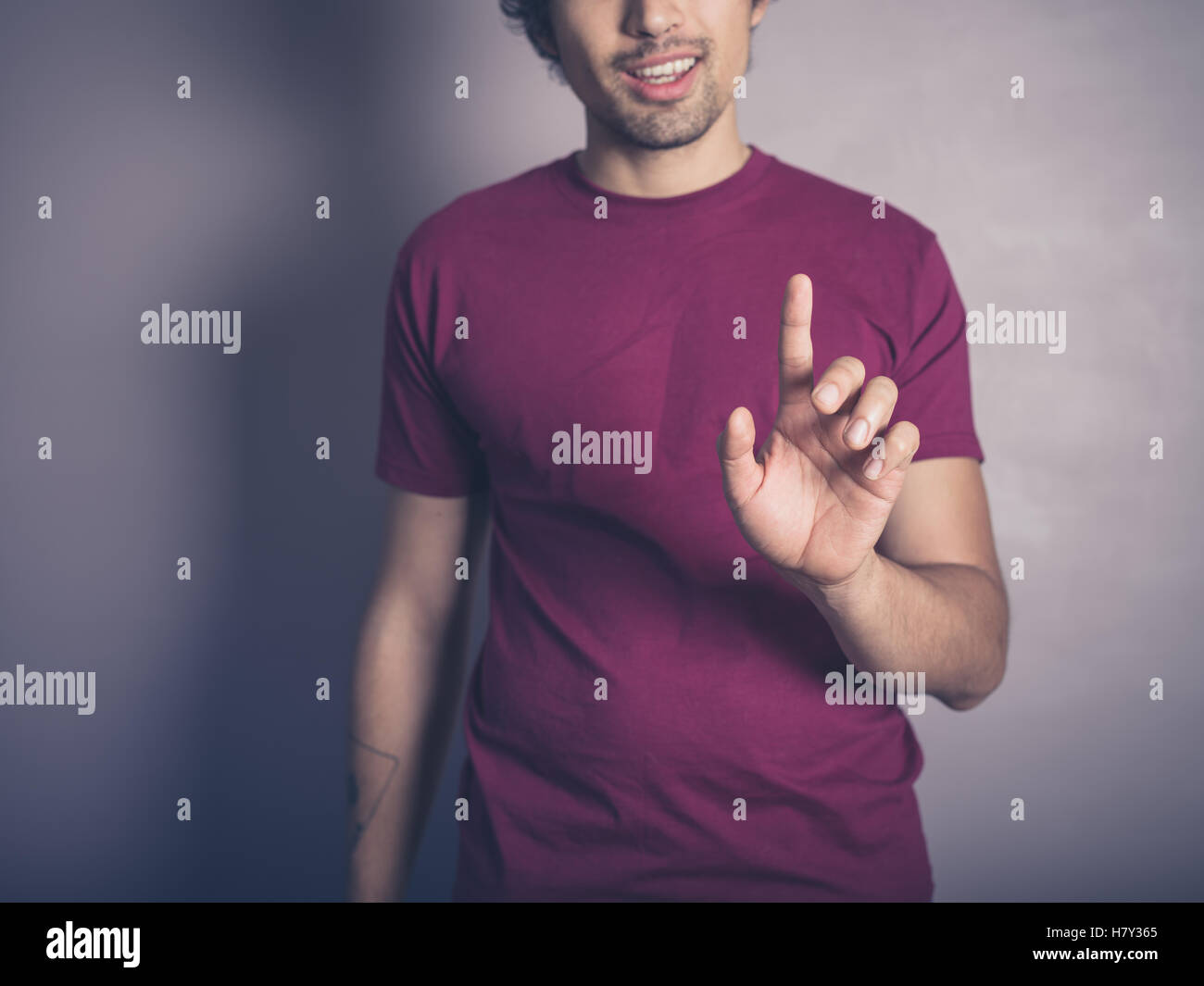 A young man in purple is raising his finger to swipe, push or establish ...