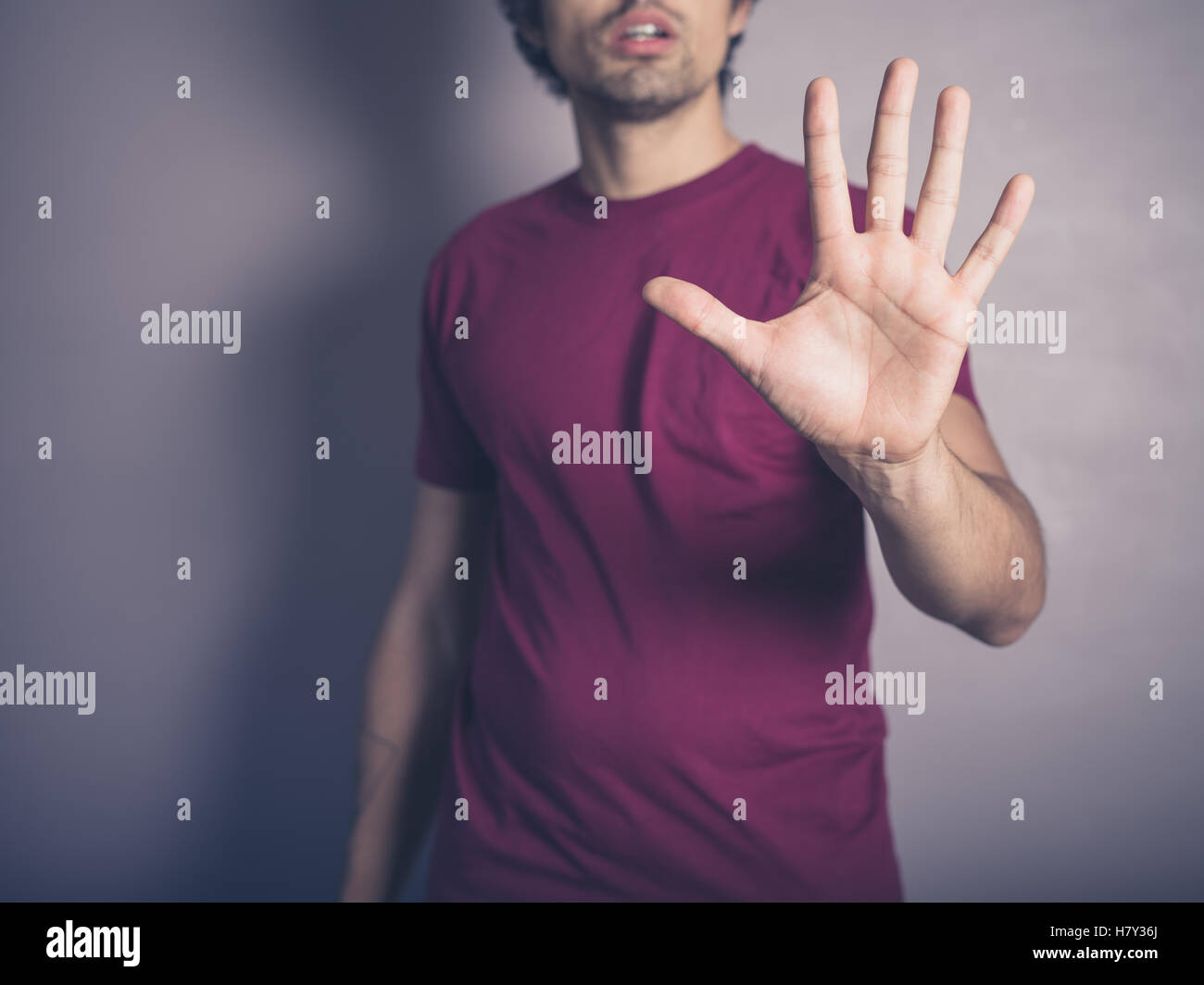A young man wearing purple is raising his open hand to signal stop ...