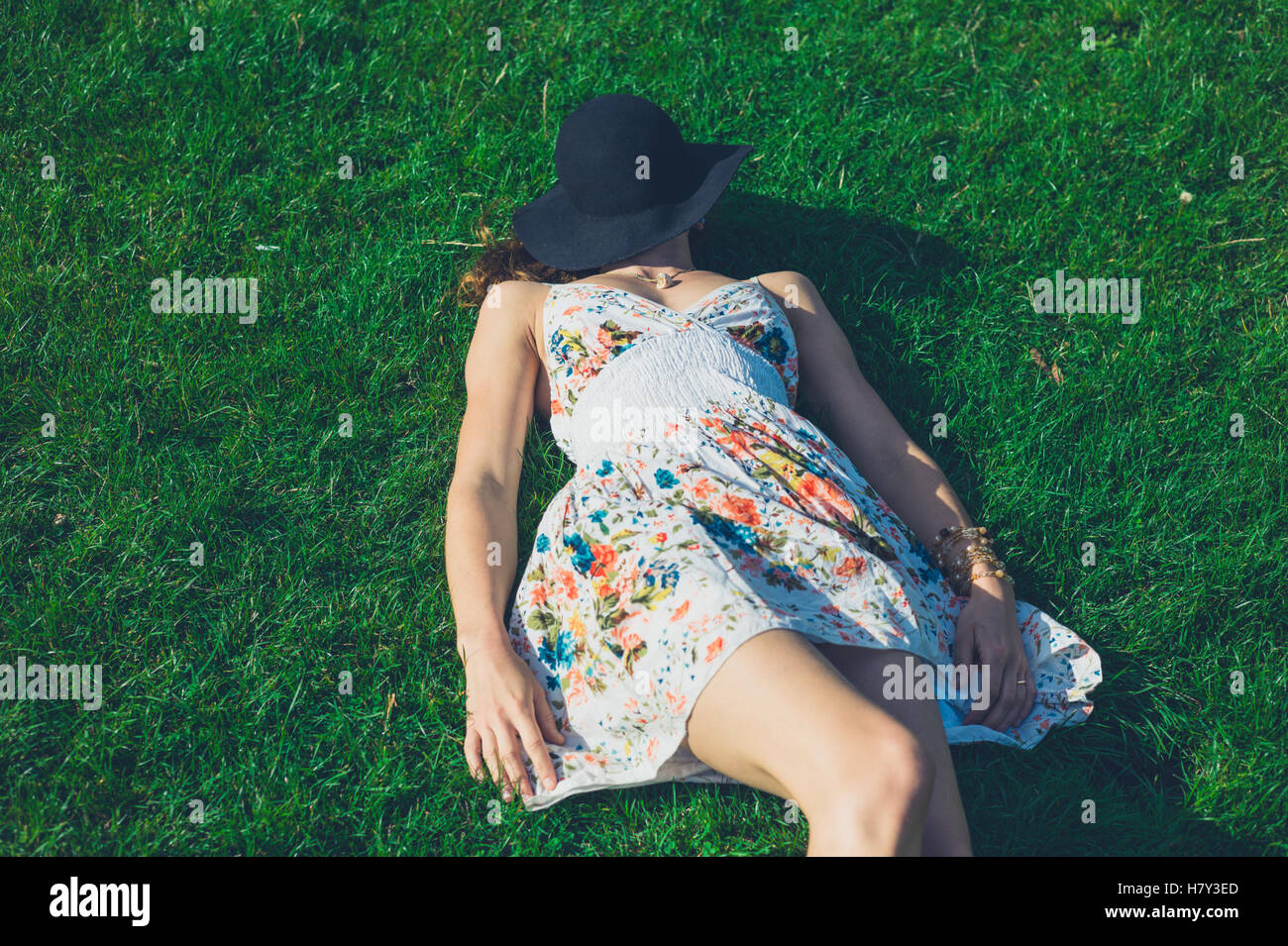 A young woman wearing a summer dress and a hat is lying on the green ...