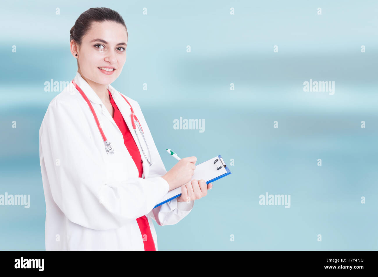 Attractive young doctor writing treatment on clipboard isolated on blue ...