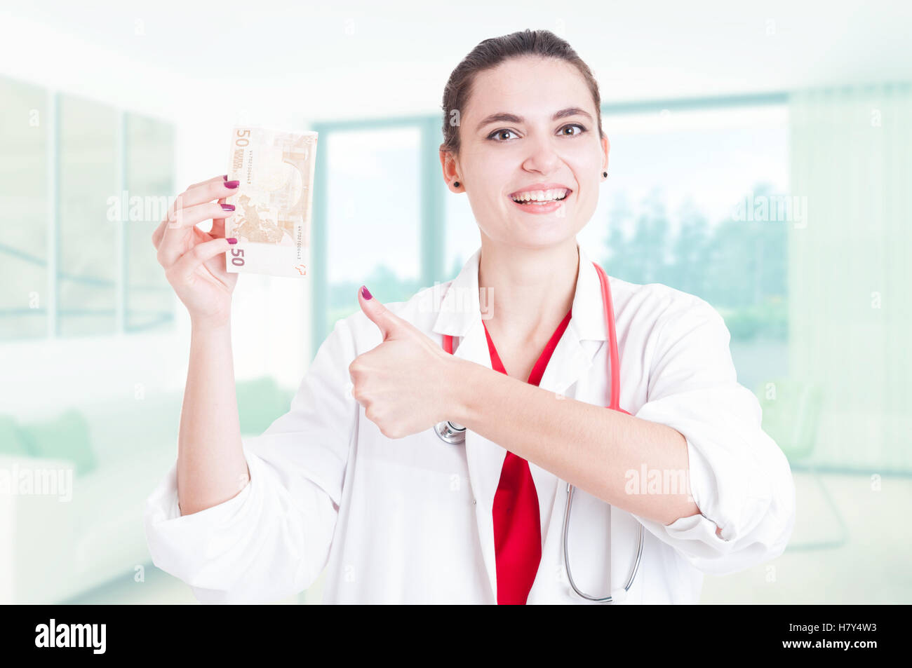 Smiling pretty medic showing thumb up and holding euro banknote as ...
