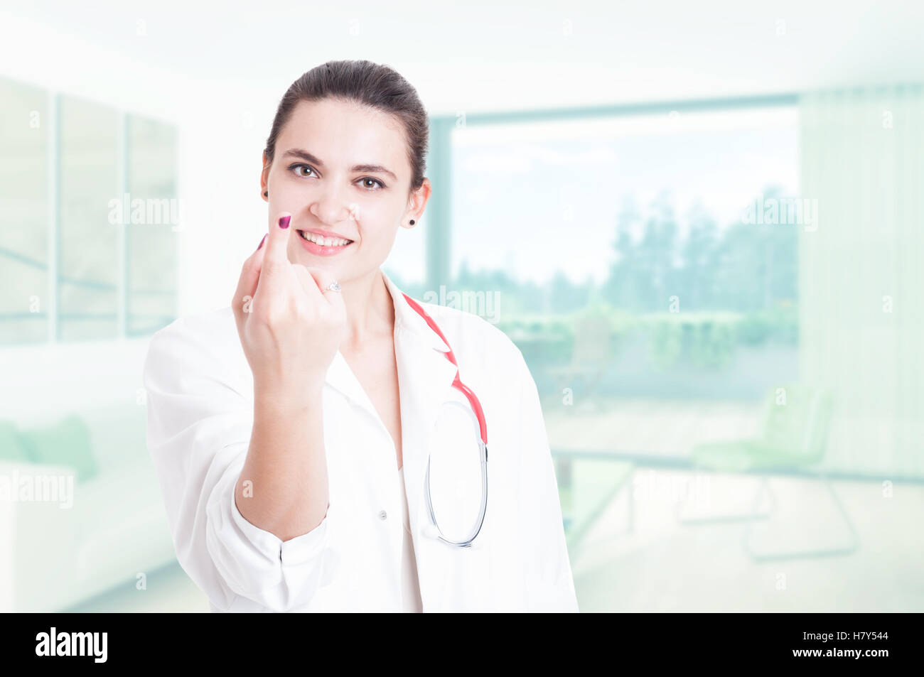 Cheerful young medic pointing finger or indicating you in her office ...