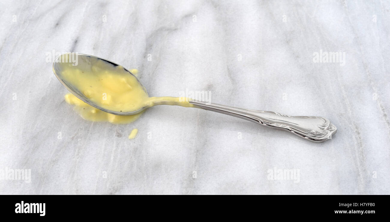 A dirty spoon with cheddar potato soup atop a marble cutting board ...