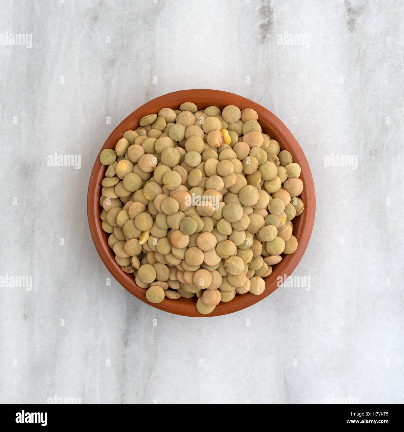 Top view of organic green lentils in a small bowl atop a gray marble ...