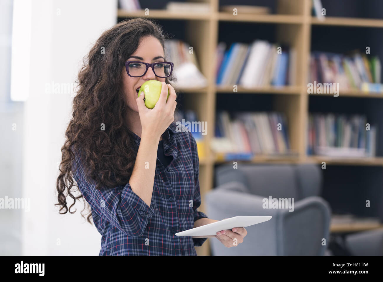 Trendy young woman eating a green apple. Over library background Stock ...