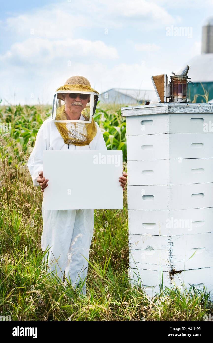 beekeeper standing beside beehive holding blank sign Stock Photo - Alamy