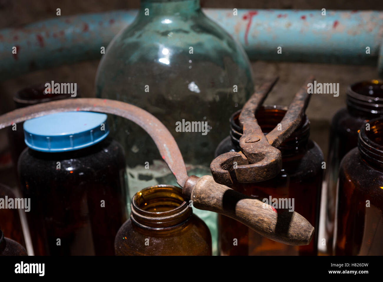 Glass jars, sickle and tongs with blood spattered wall in stained ...