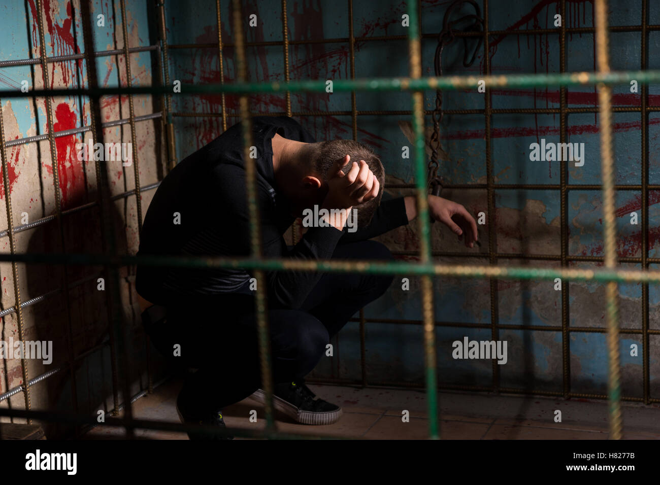 Male victim imprisoned in a metal cage with a blood splattered wall ...