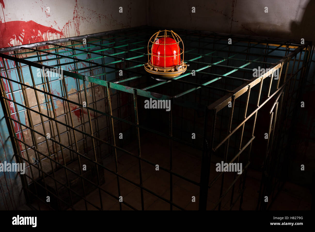 Red lamp on the iron cage behind blood splattered wall for concept ...