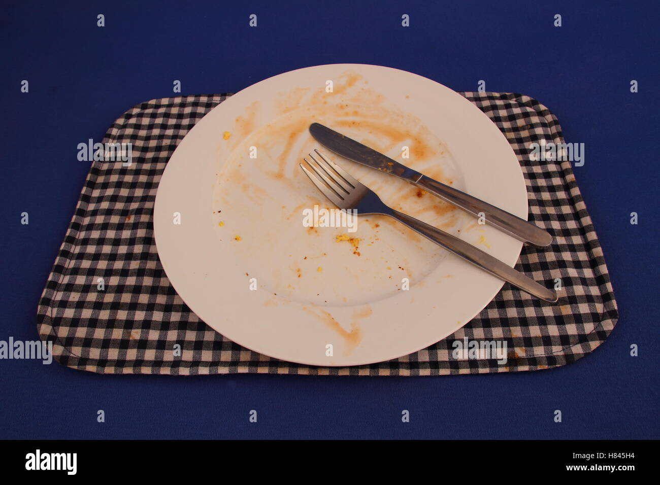 Dirty dinner plate after a meal isolated on a blue and white checked ...