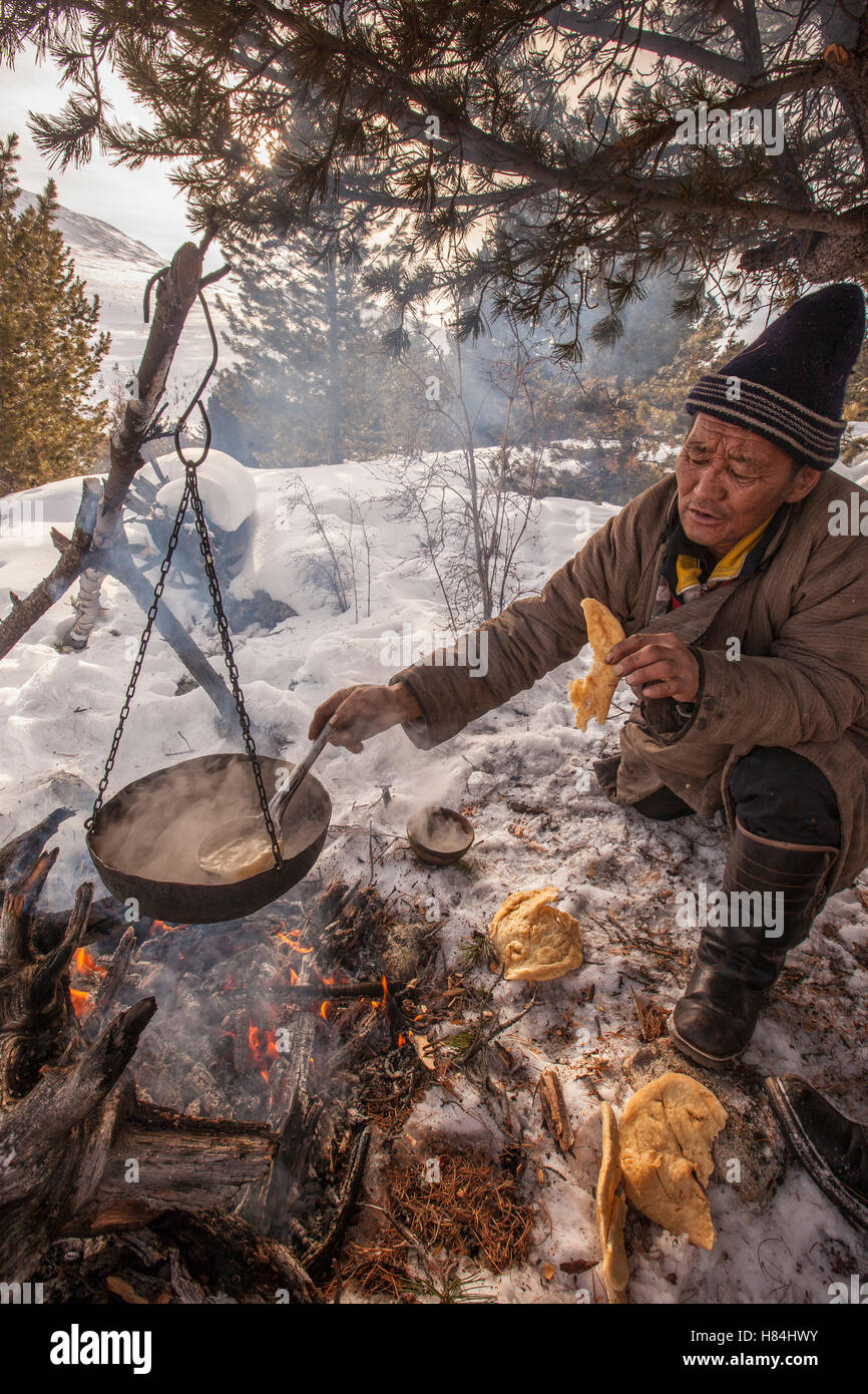 Tsataan man making tea in taiga forest while bread cooks beside the ...