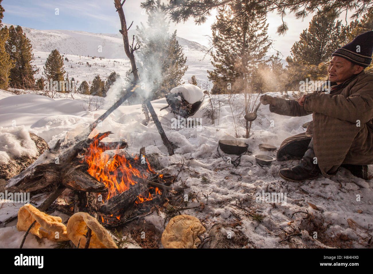 Tsataan man making tea in taiga forest while bread cooks beside the ...