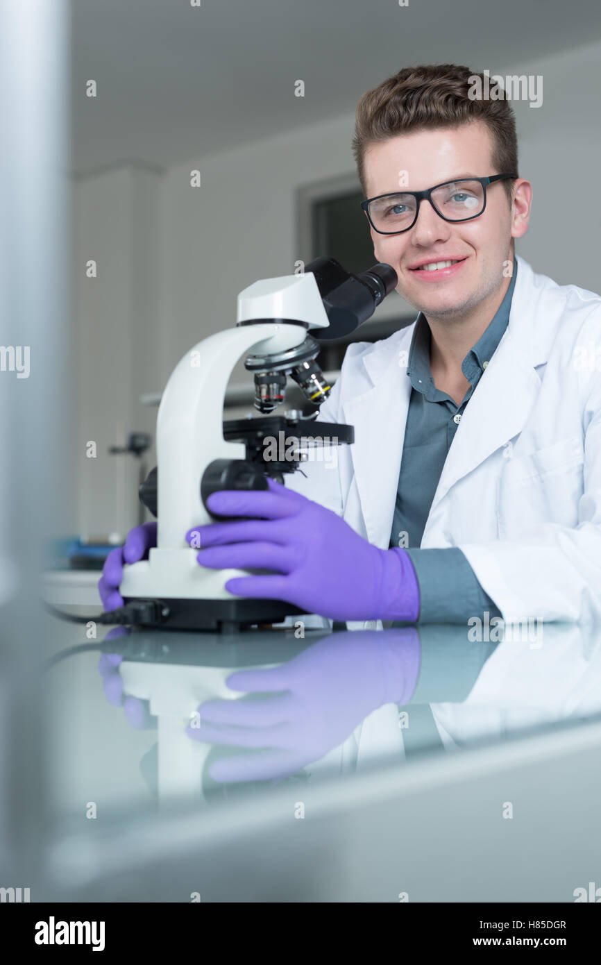 Young scientist investigating microbiological substance in microscope ...