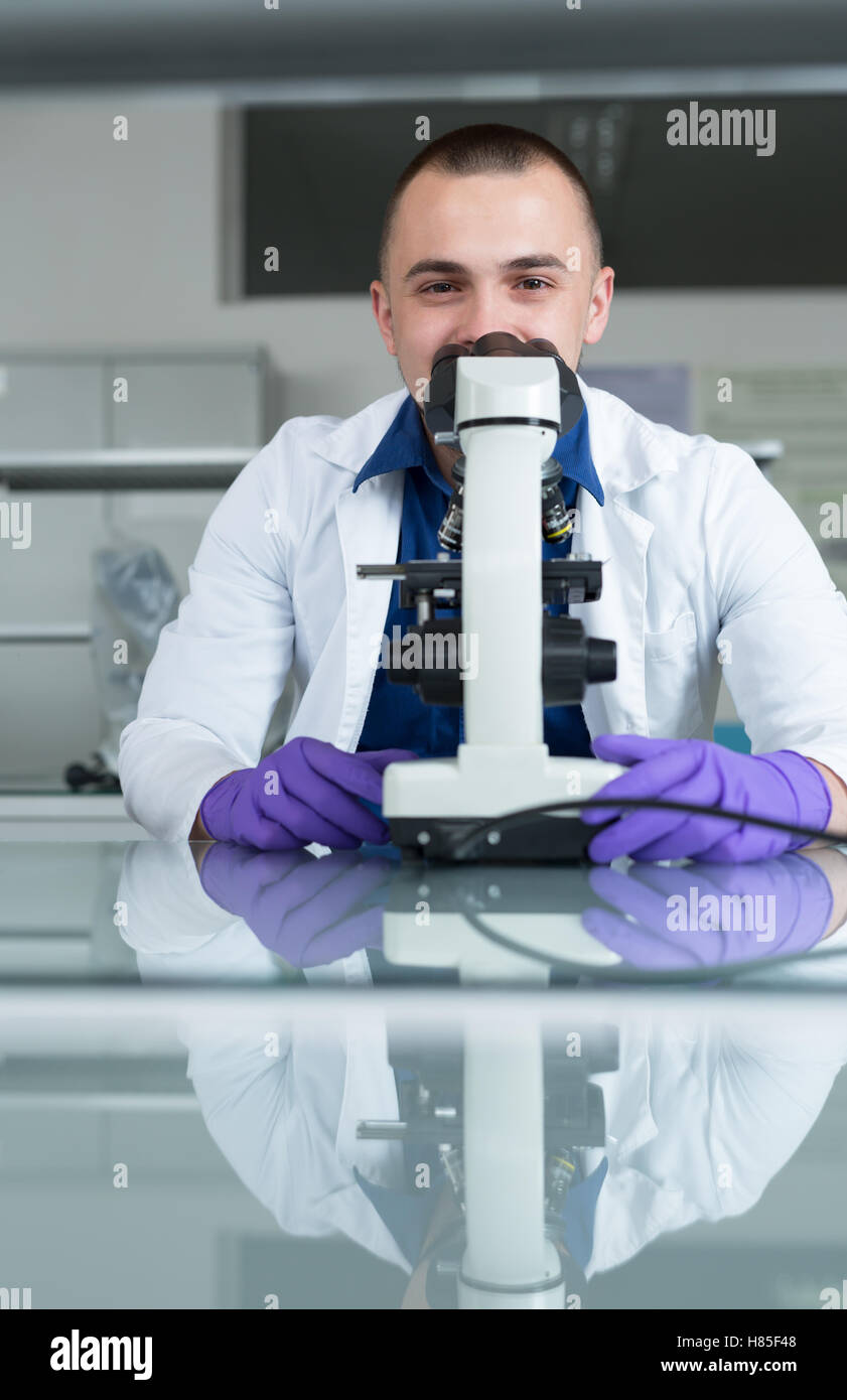 Young scientist investigating microbiological substance in microscope ...
