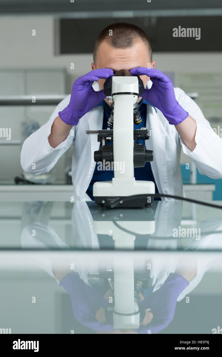 Young scientist investigating microbiological substance in microscope ...