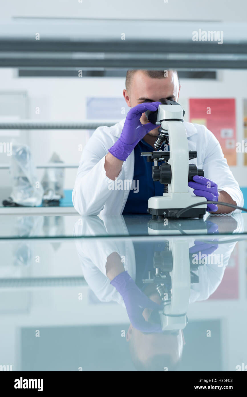 Young scientist investigating microbiological substance in microscope ...