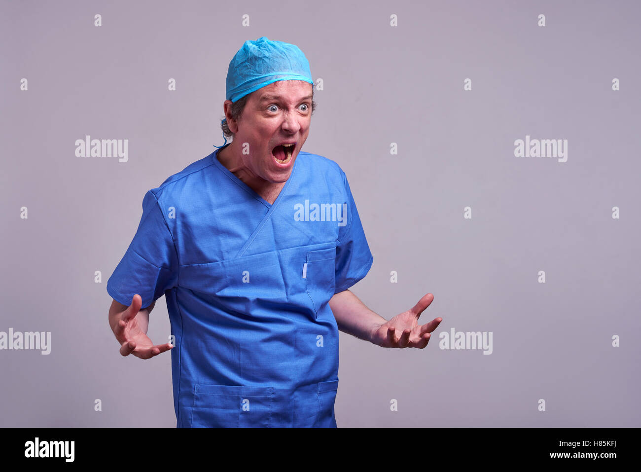 An angry middle aged male doctor standing in a blue scrubs and ...
