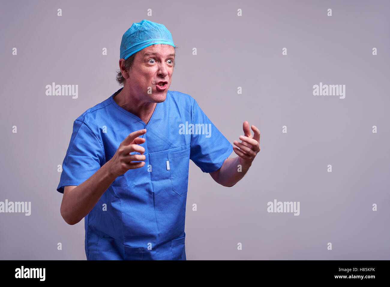 An angry middle aged male doctor standing in a blue scrubs and ...