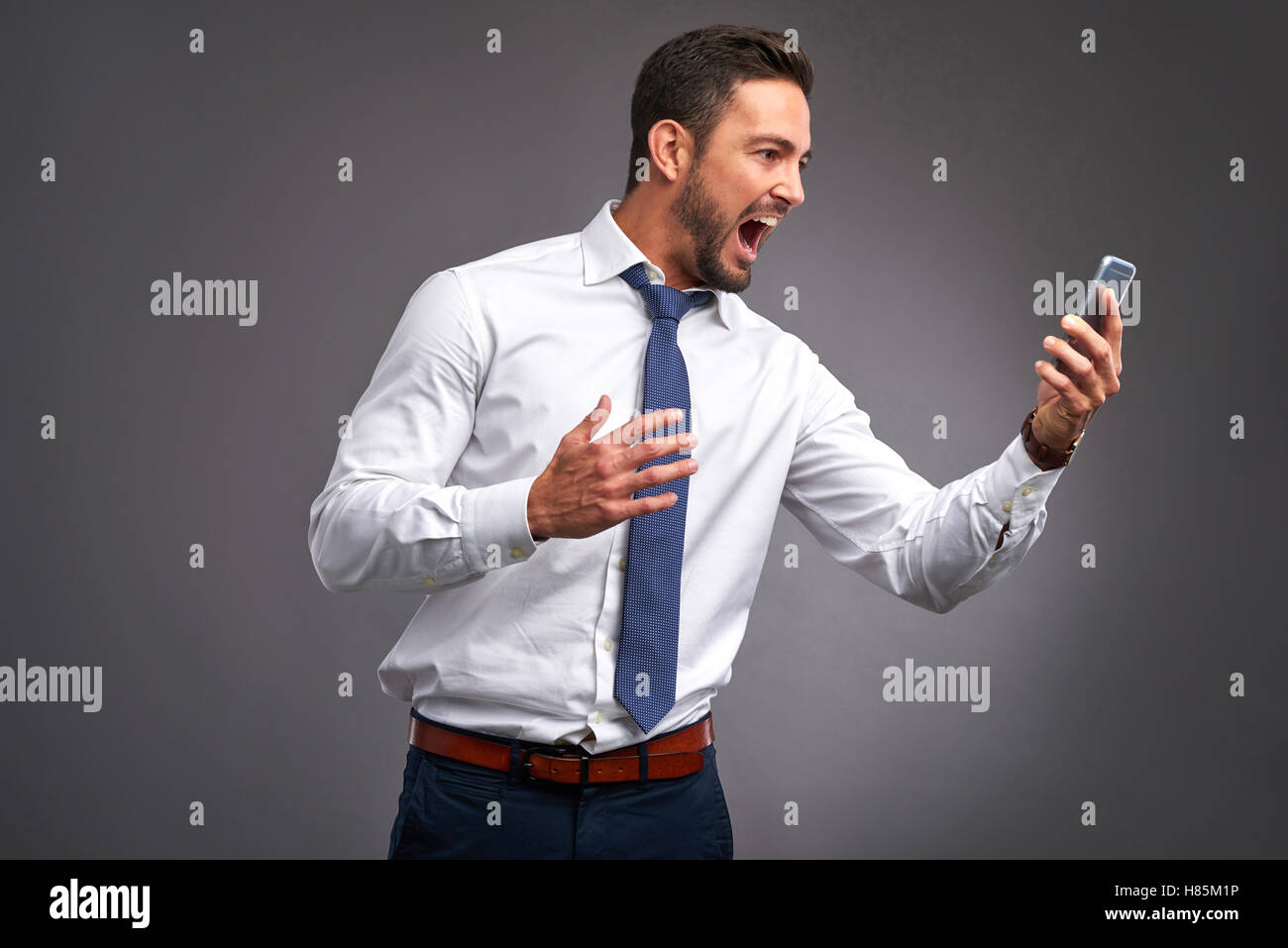 A handsome young man holding his phone and screaming to it wearing a ...