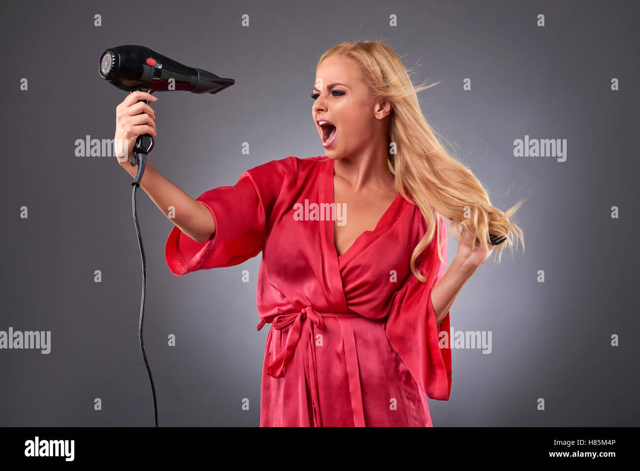 A beautiful young woman wearing a pink robe and screaming while using a ...