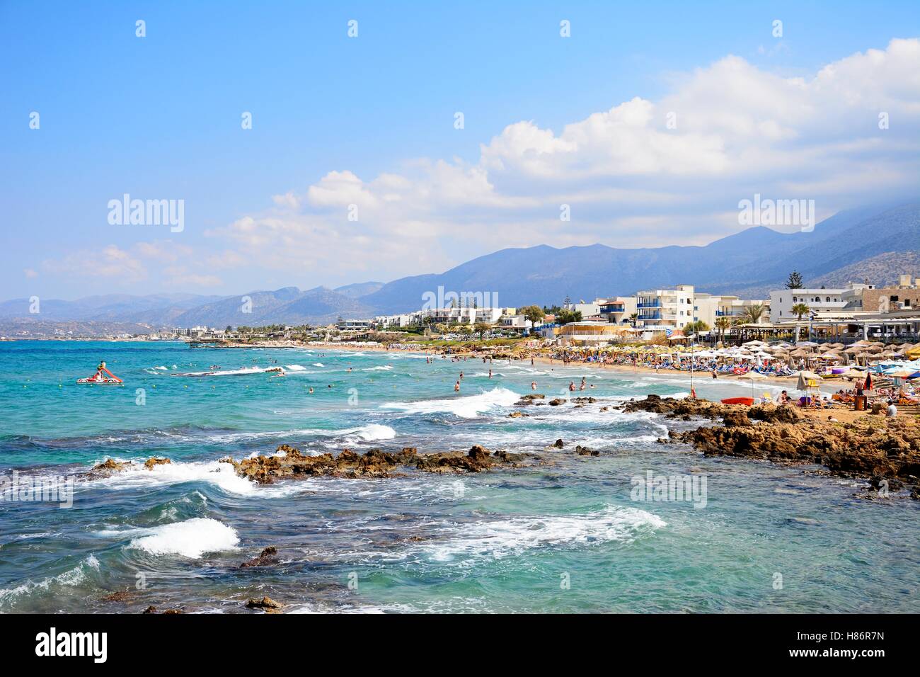 Tourists relaxing on the beach and in the sea with apartments and ...