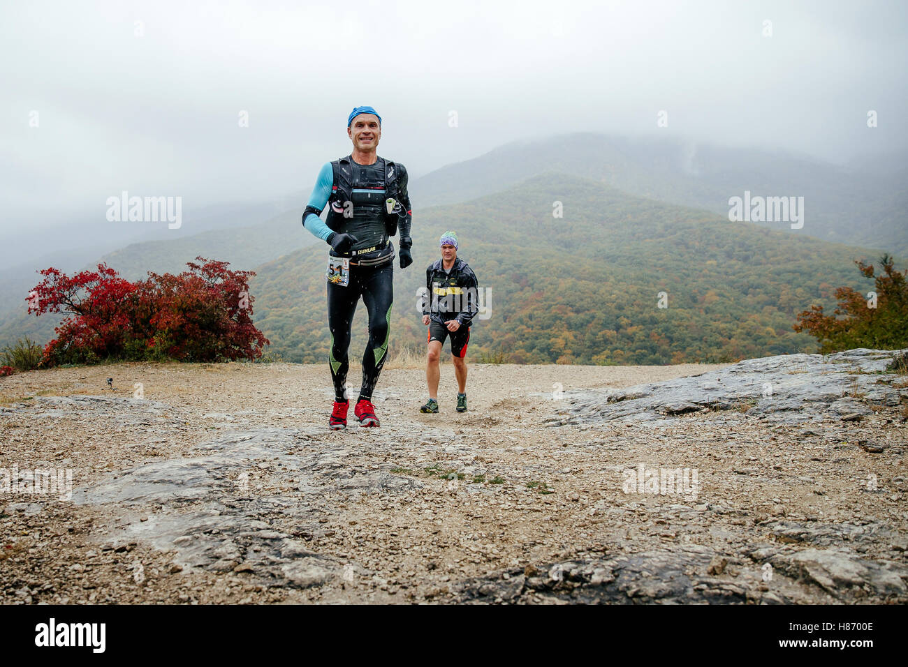 two runners middle-aged men running in rain on a mountain trail during ...