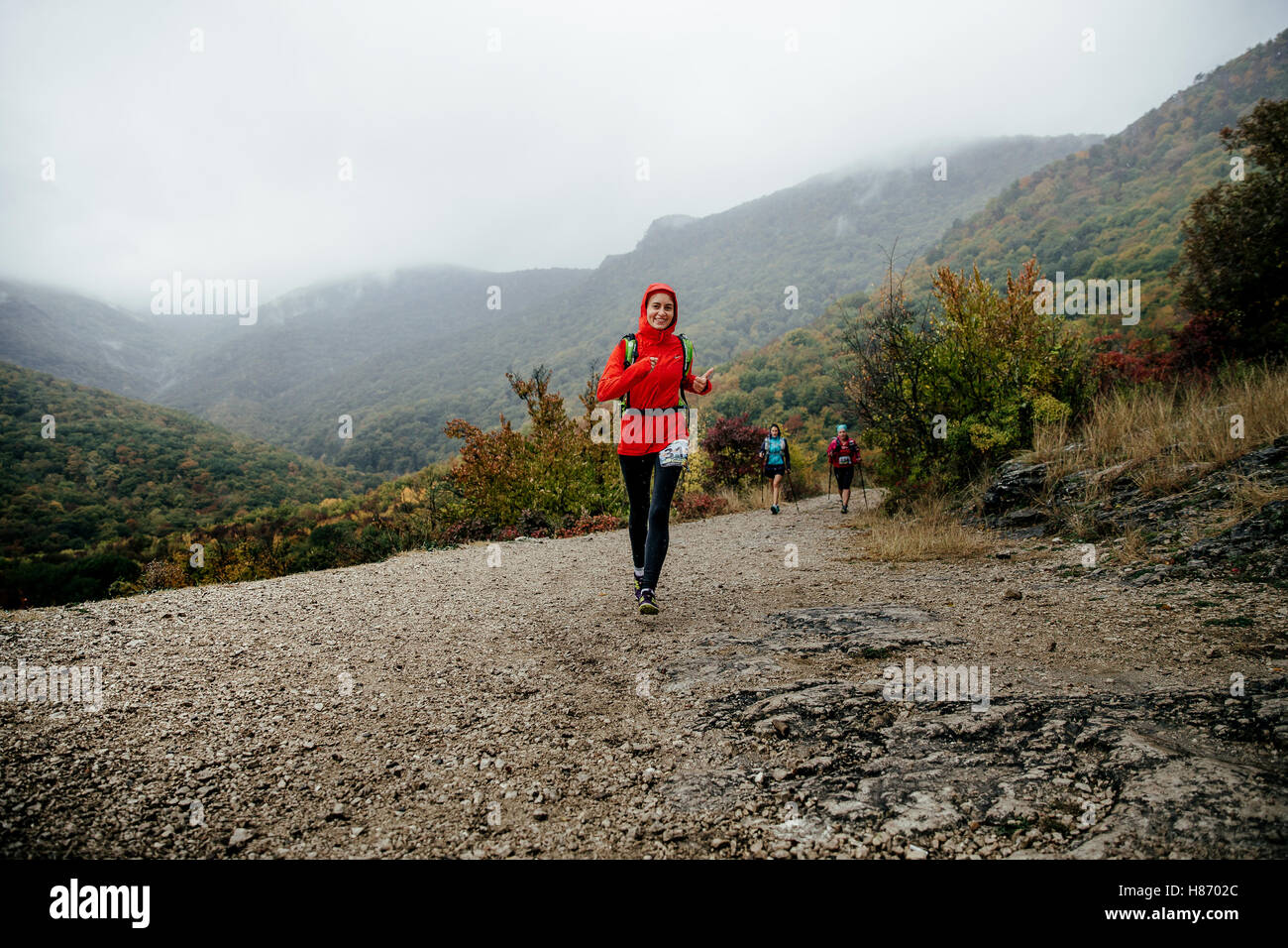 young girl runner running in rain in a red jacket with a smile on face ...