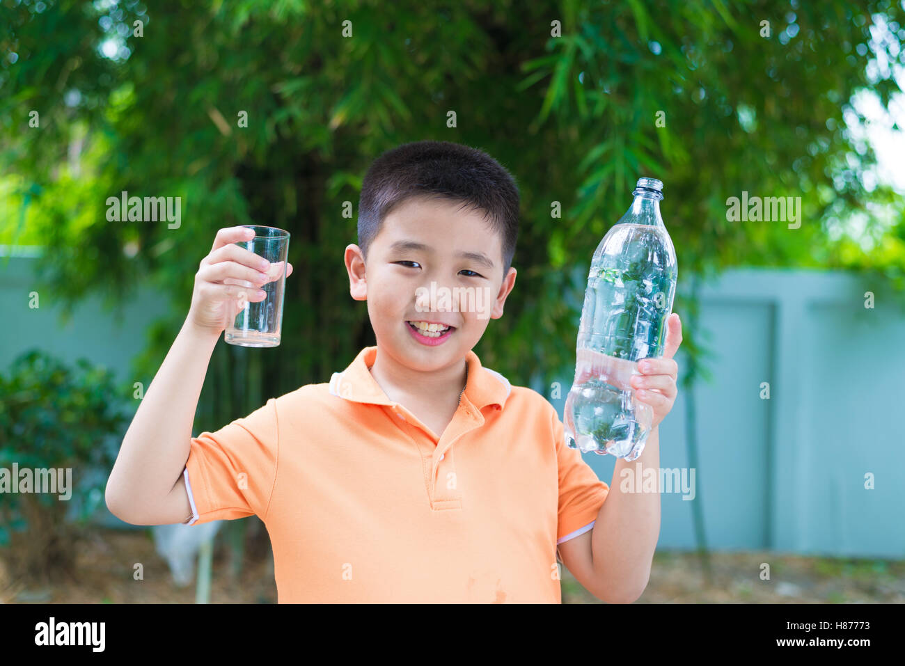 Asian boy pouring water into glass from bottle, in garden, green ...