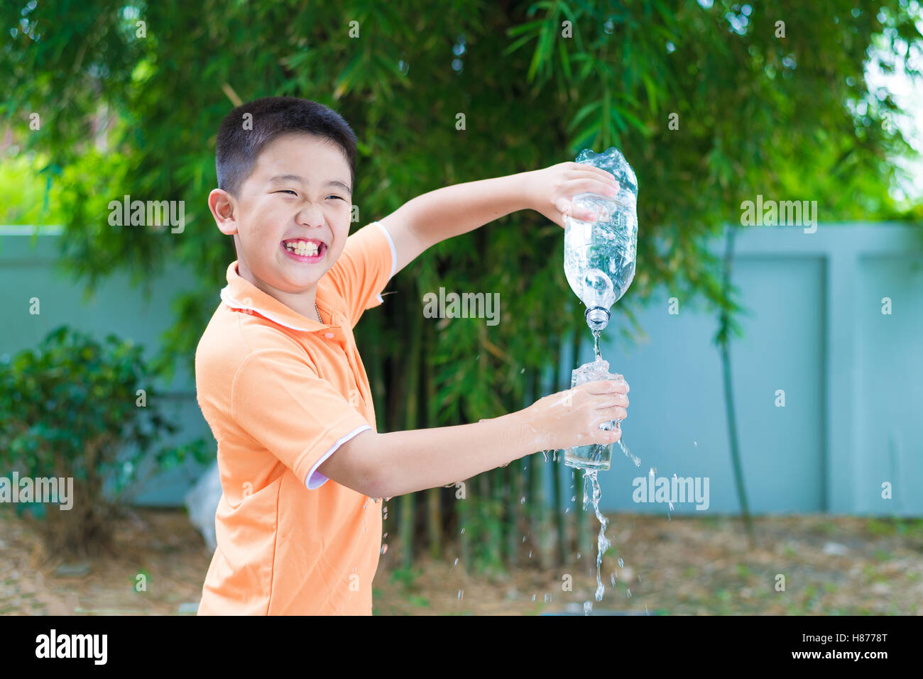 Asian boy pouring water into glass from bottle, in garden, green ...