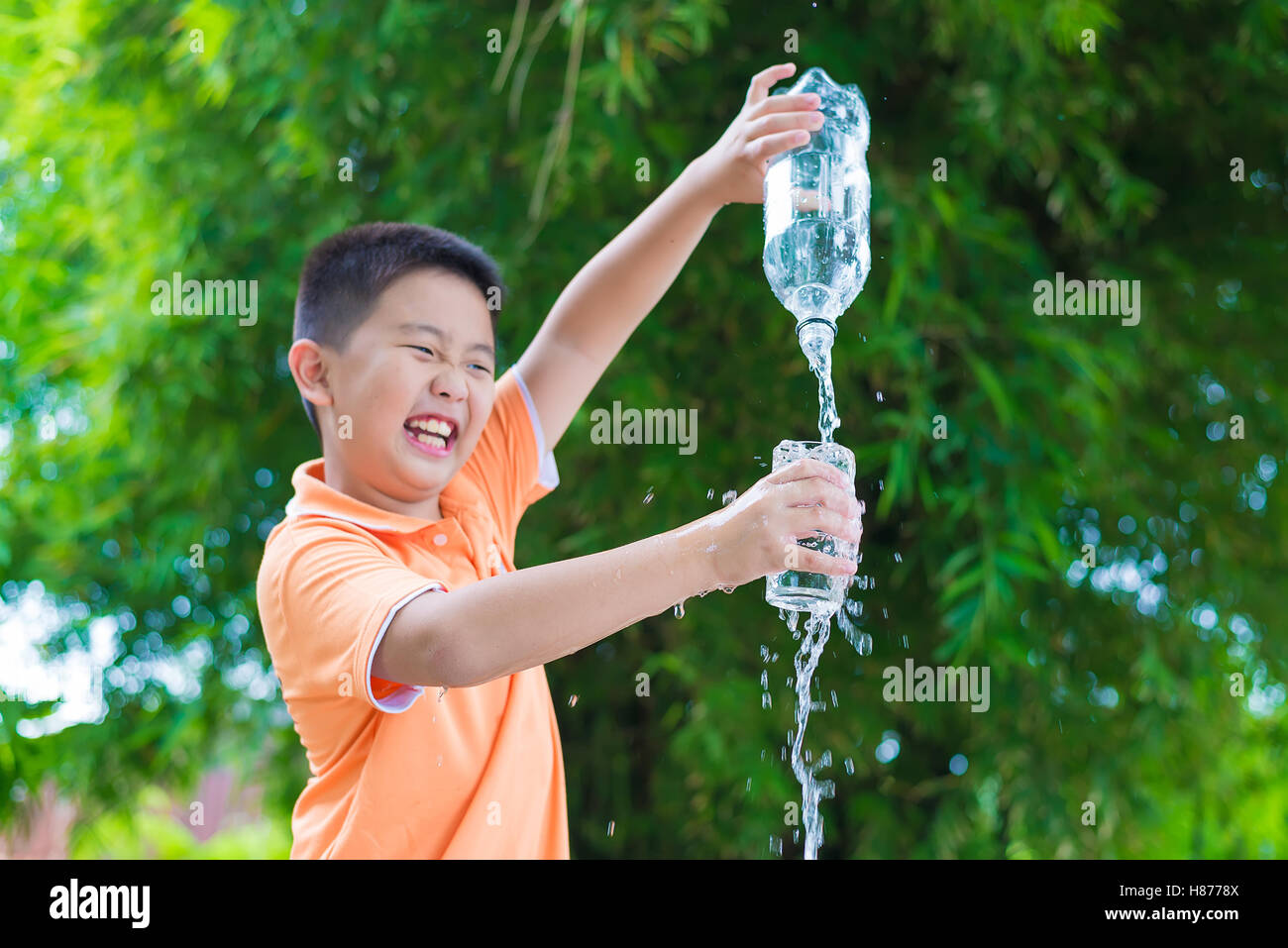 Asian boy pouring water into glass from bottle, in garden, green ...