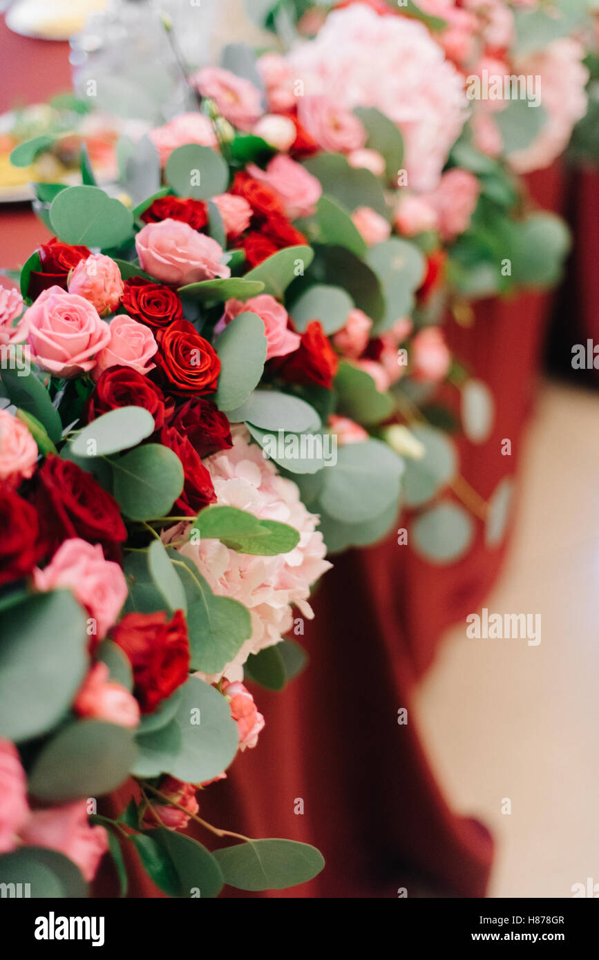 Flower festoon with greenery lies on red dinner table Stock Photo - Alamy