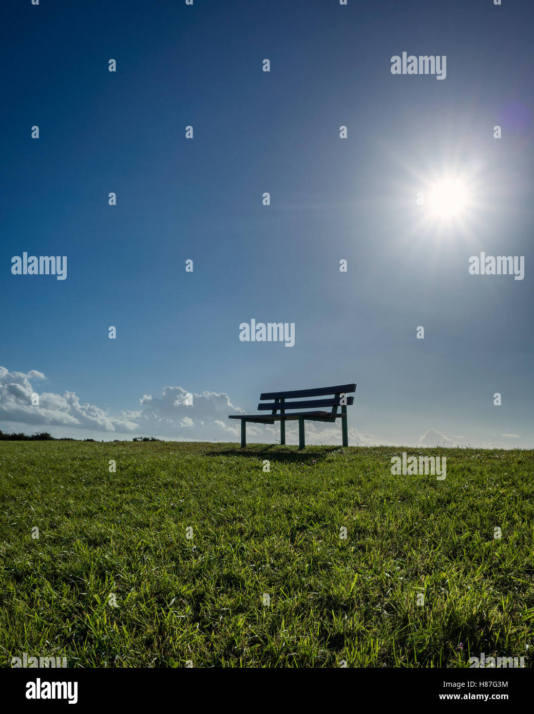 A lone bench on dyke looks surreal with low clouds and sun behind ...