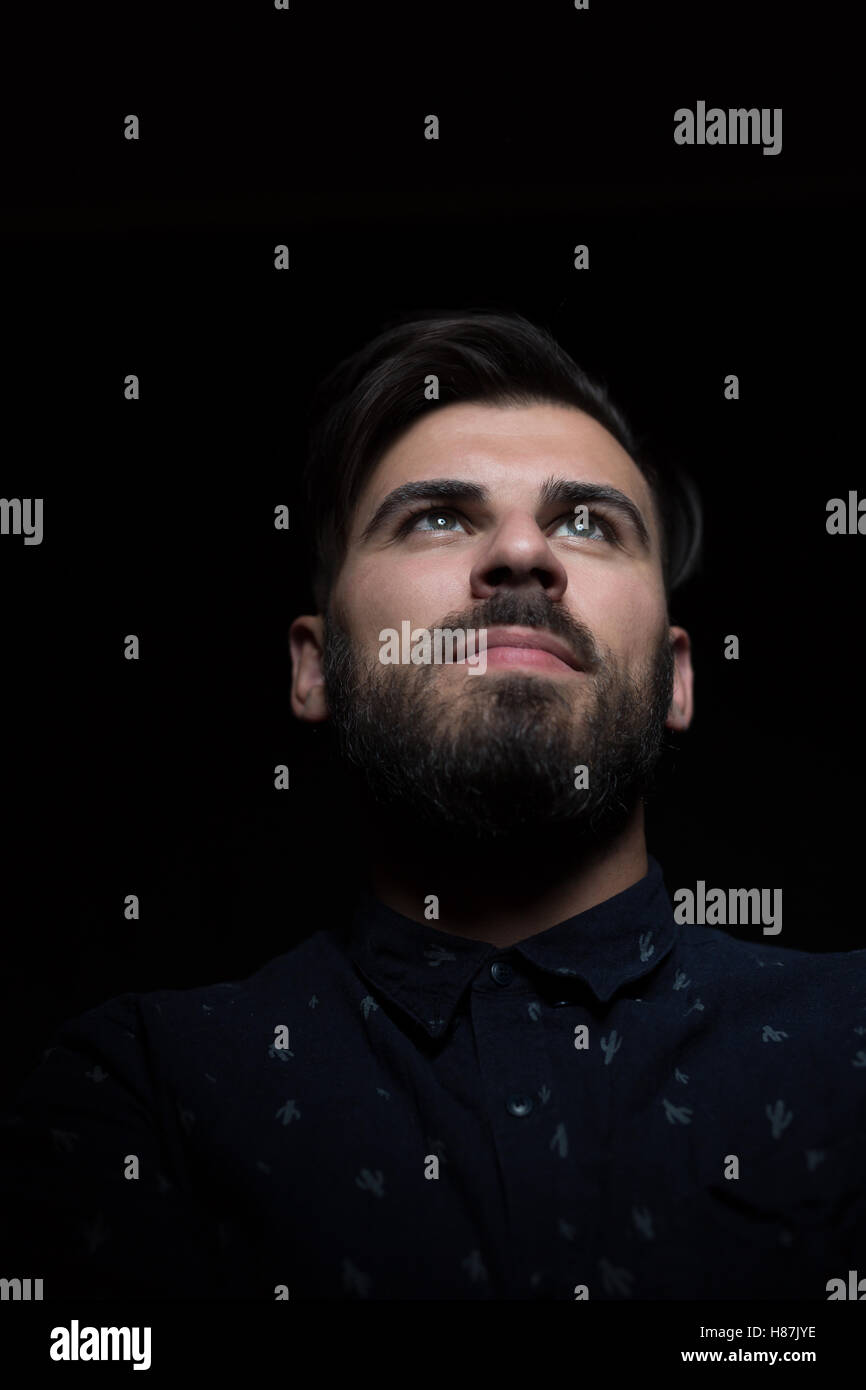 low key portrait of young handsome man in dark shirt isolated on black ...