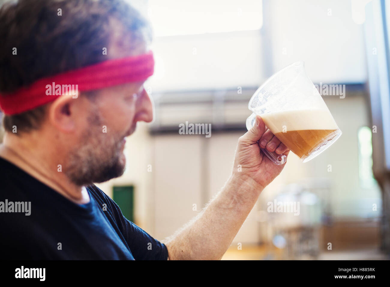 A brewer with a red bandana taking a jug of brewing beer and examining ...