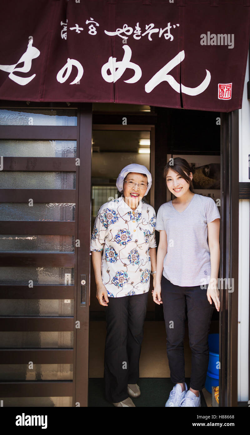 Two women at a noodle shop, a small unit with a fast food kitchen and ...