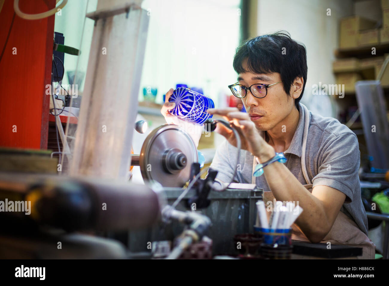 A craftsman at work in a glass maker's workshop polishing a vivid blue ...