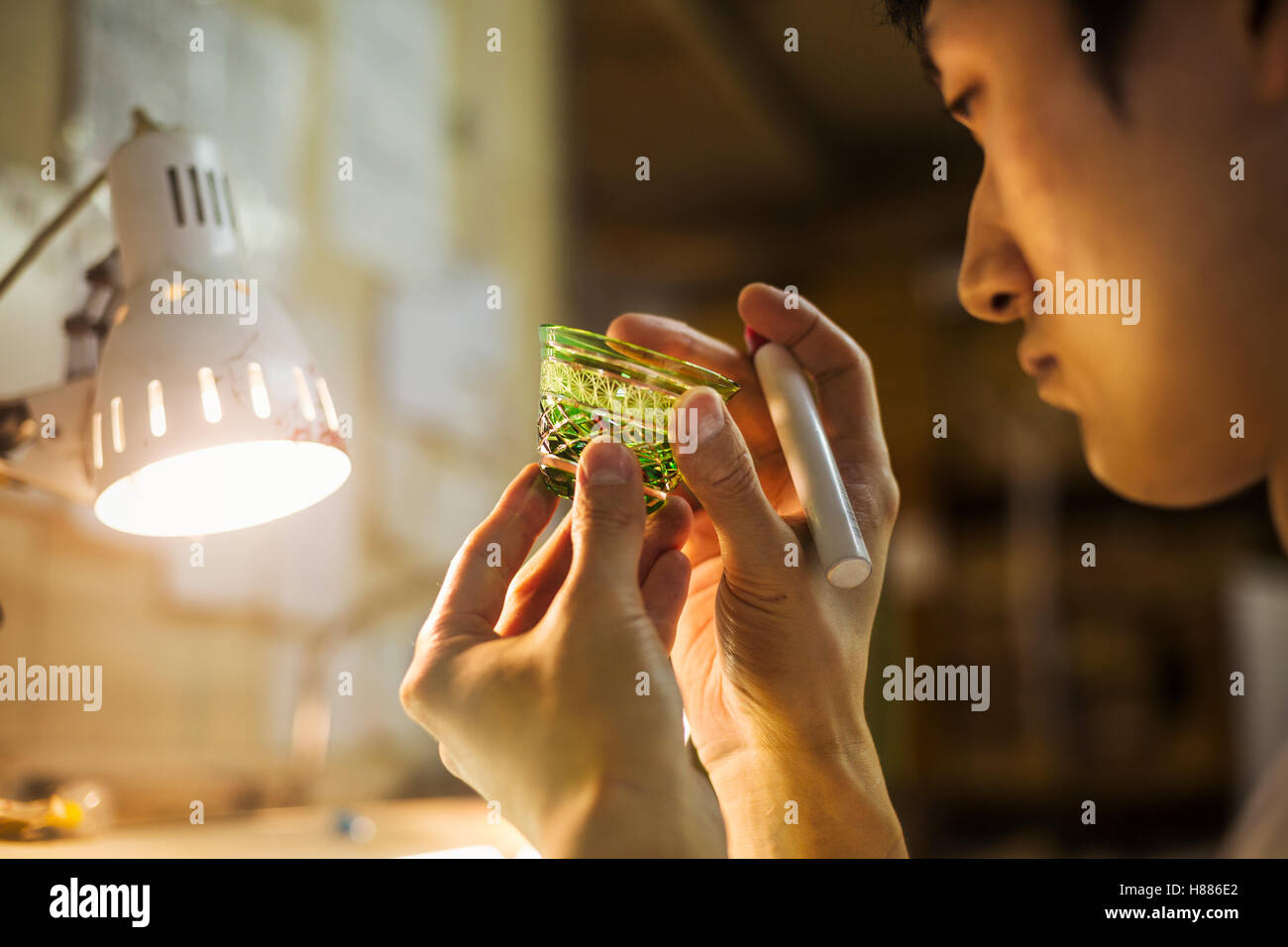 A craftsman at work in a glass maker's studio workshop, inspecting a ...
