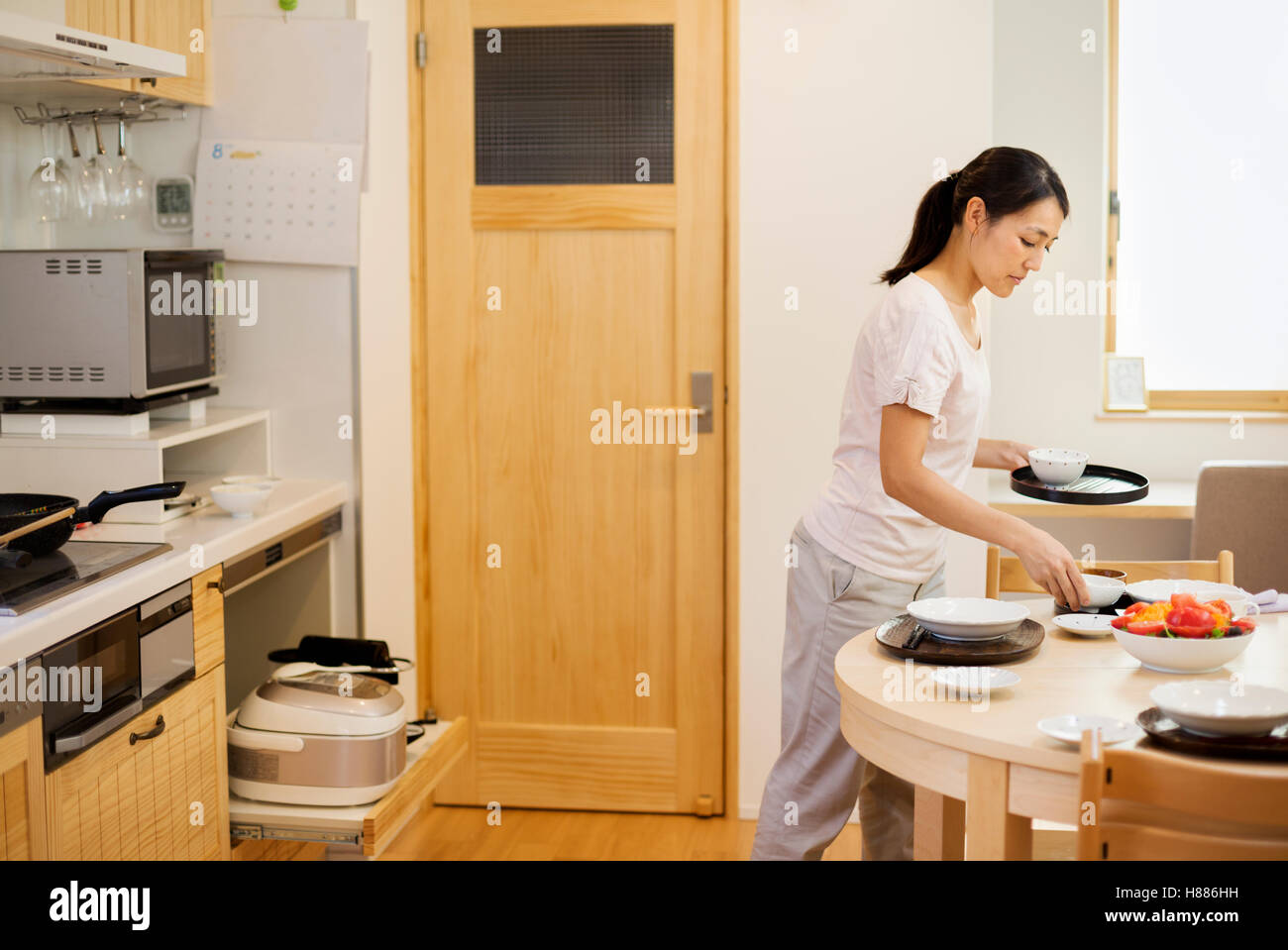Family home. A woman preparing a meal in a kitchen, placing dishes on ...