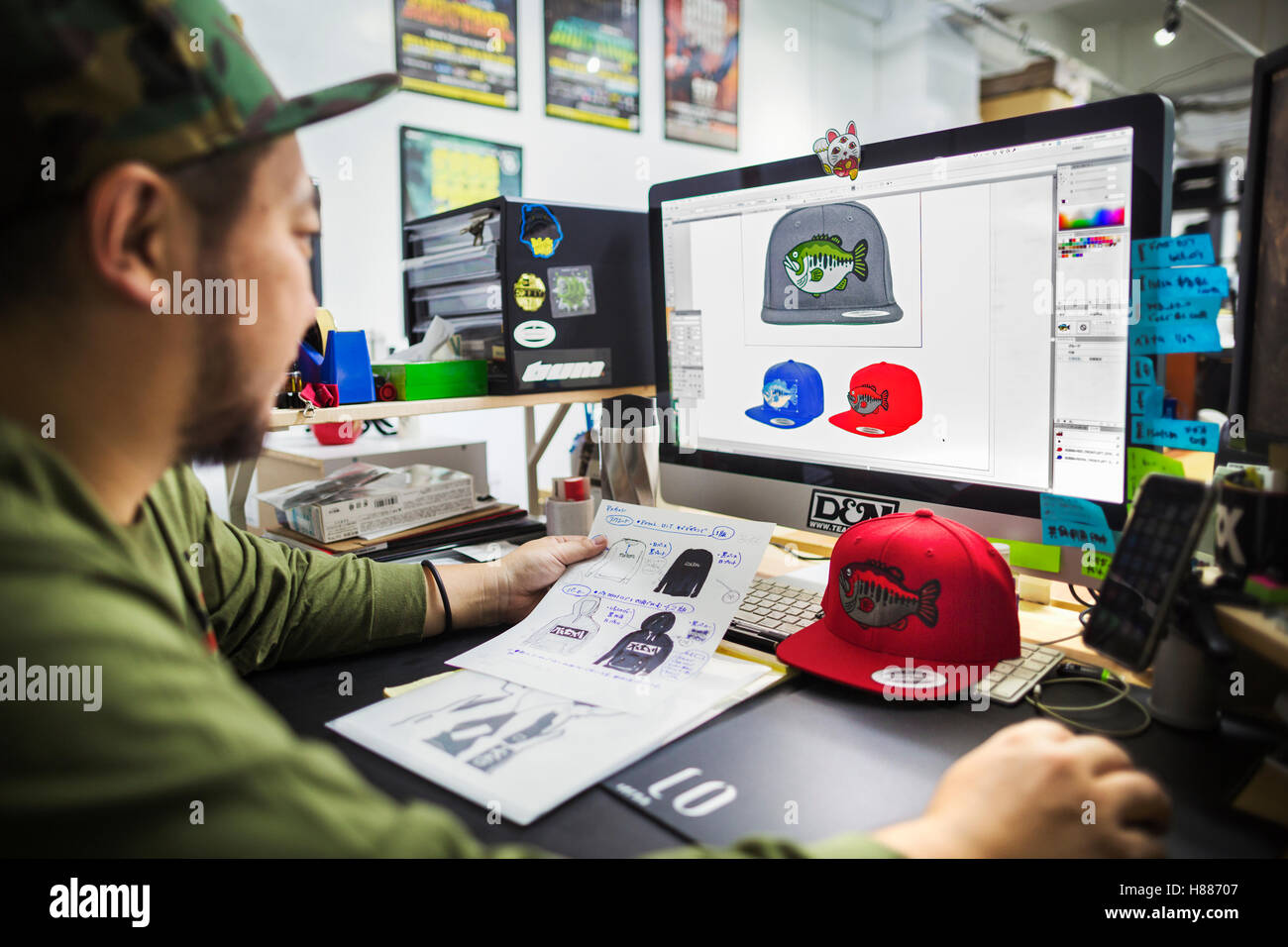 A man, a designer working on screen creating designs for baseball caps ...