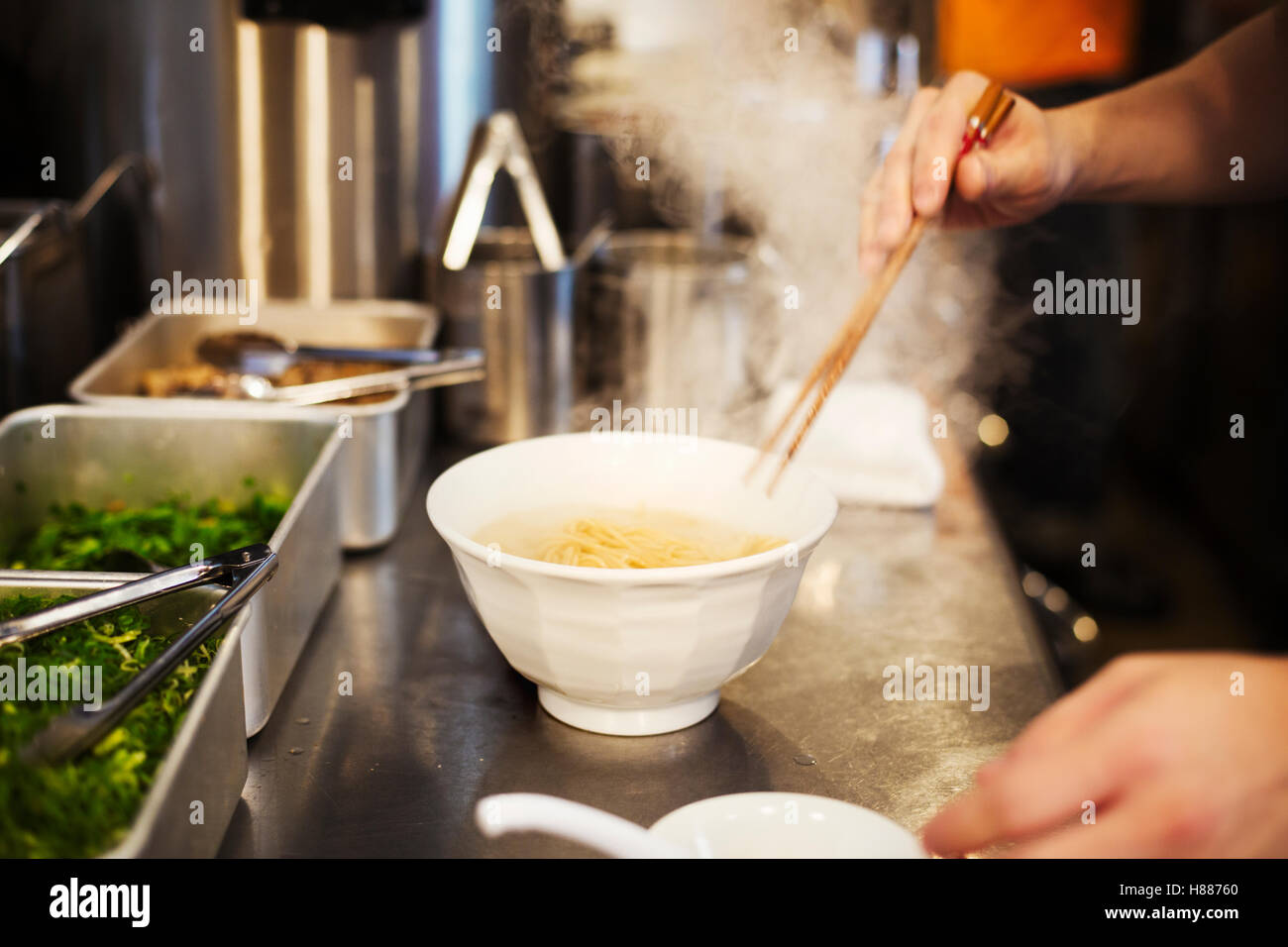 A ramen noodle shop kitchen. A chef preparing bowls of ramen noodles in ...