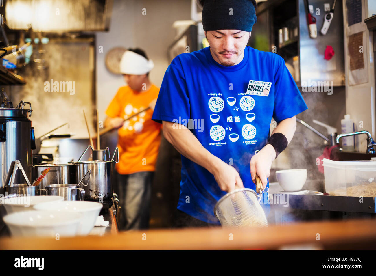 A ramen noodle shop kitchen. A chef preparing bowls of ramen noodles in ...